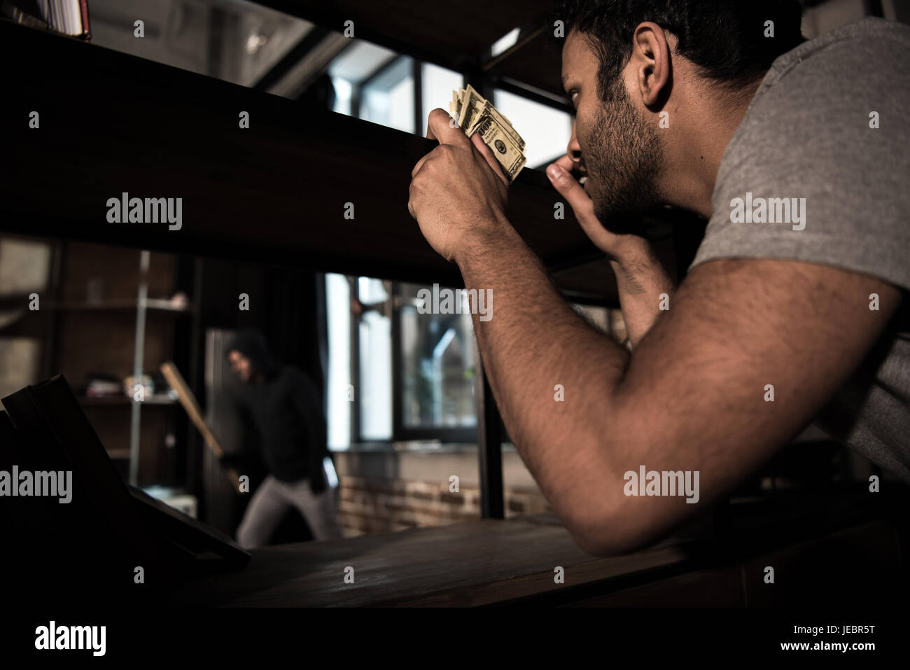 Scared man with money hiding from burglar behind bookshelves, house ...