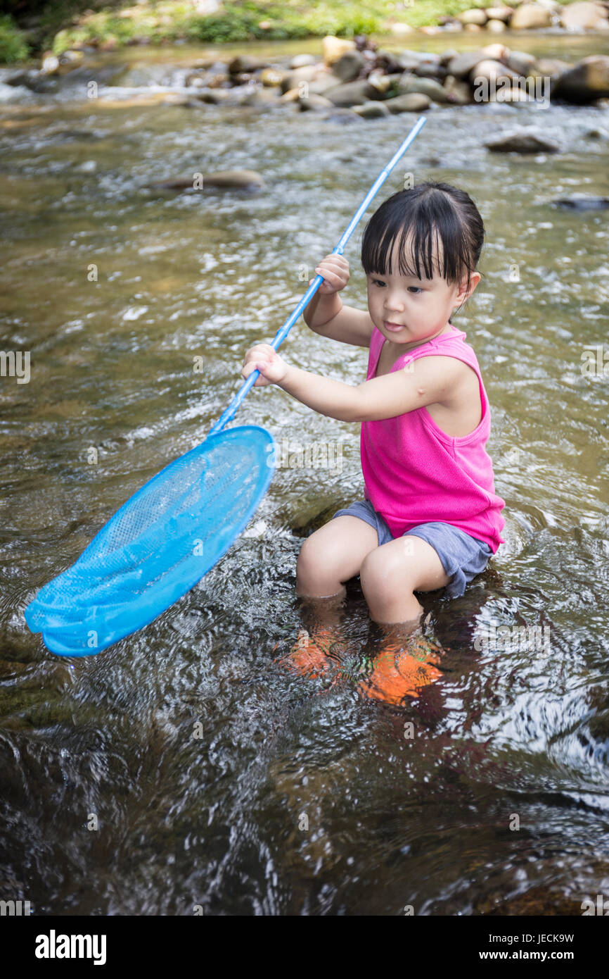 Asian Chinese little girl catching fish with fishing net in the creek ...