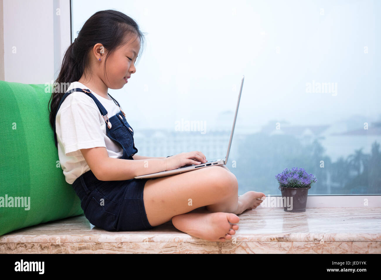 Asian Chinese little girl using laptop on the windowsill at home Stock ...
