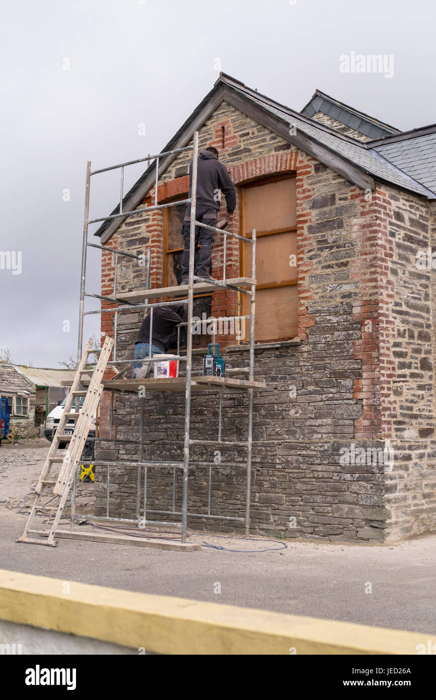 Traditional Cornish stone built building with two men repointing the ...