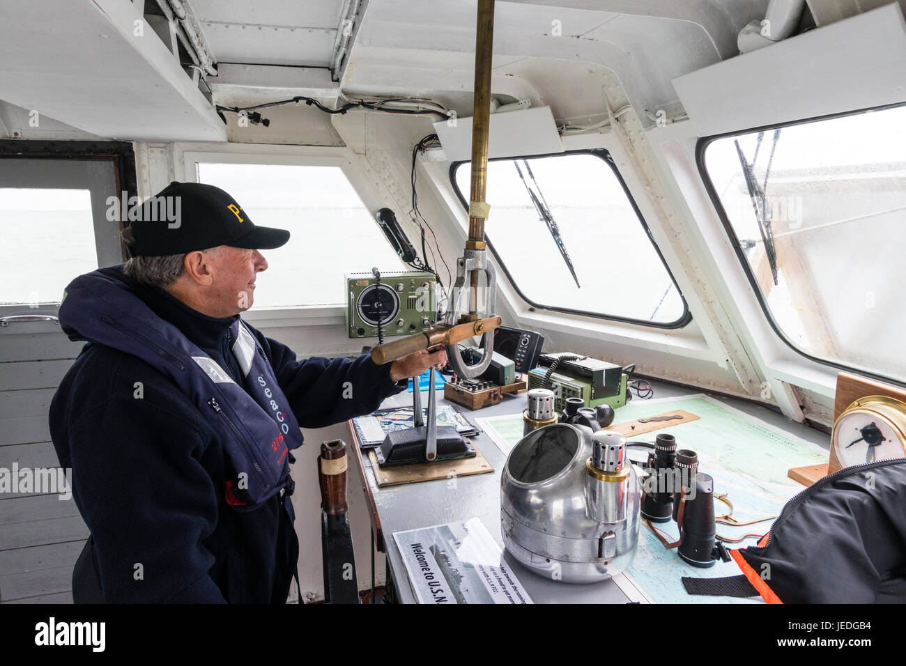 Senior man piloting boat, interior of ship's bridge, man in lifejacket ...