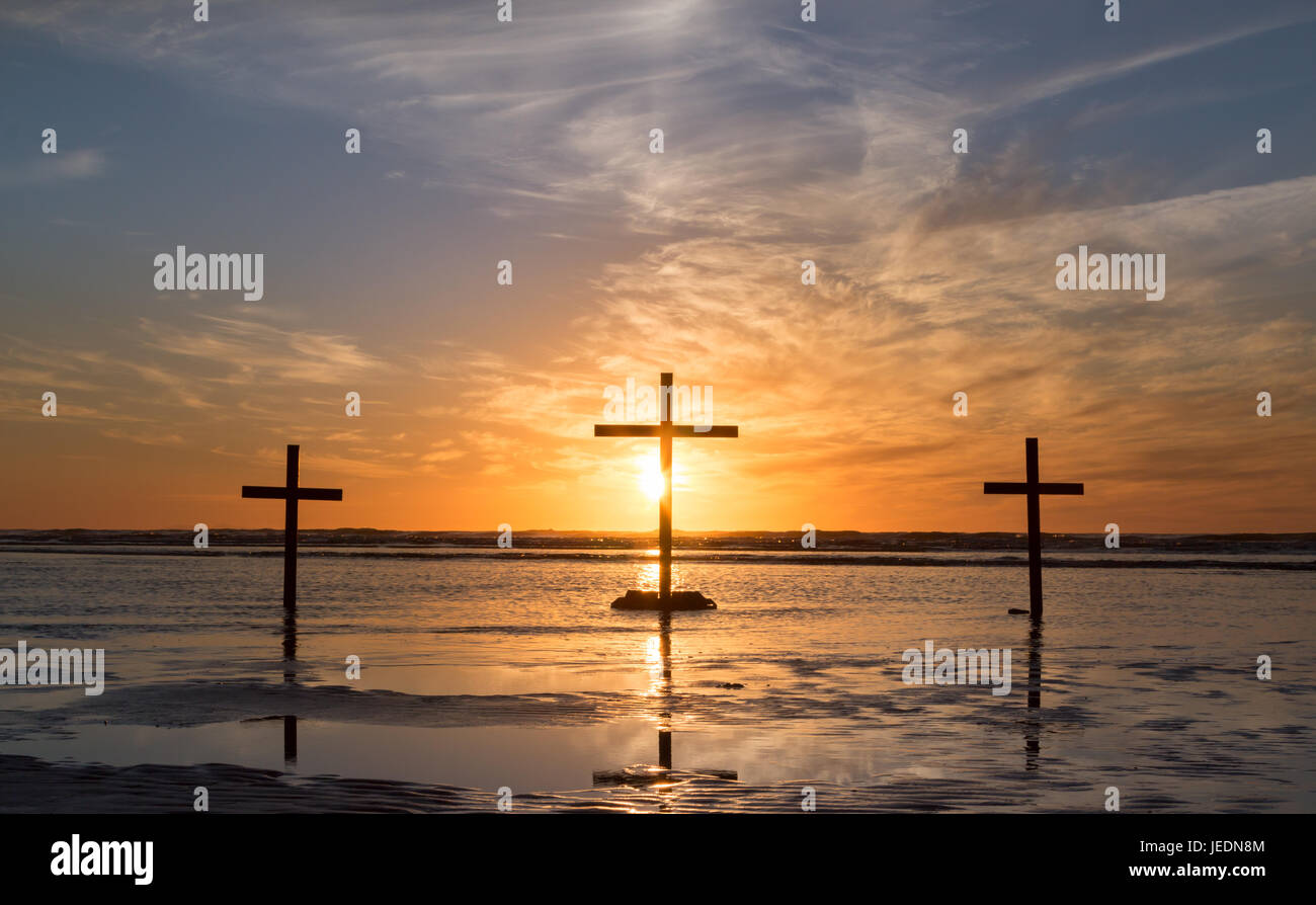 Three cross on a beach with water around them as the sunsets behind ...