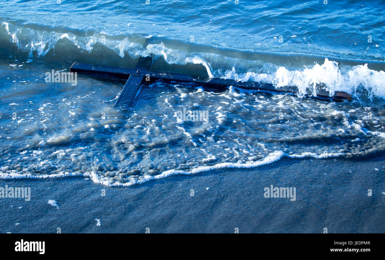 Wave washing over a black cross on a beach Stock Photo - Alamy