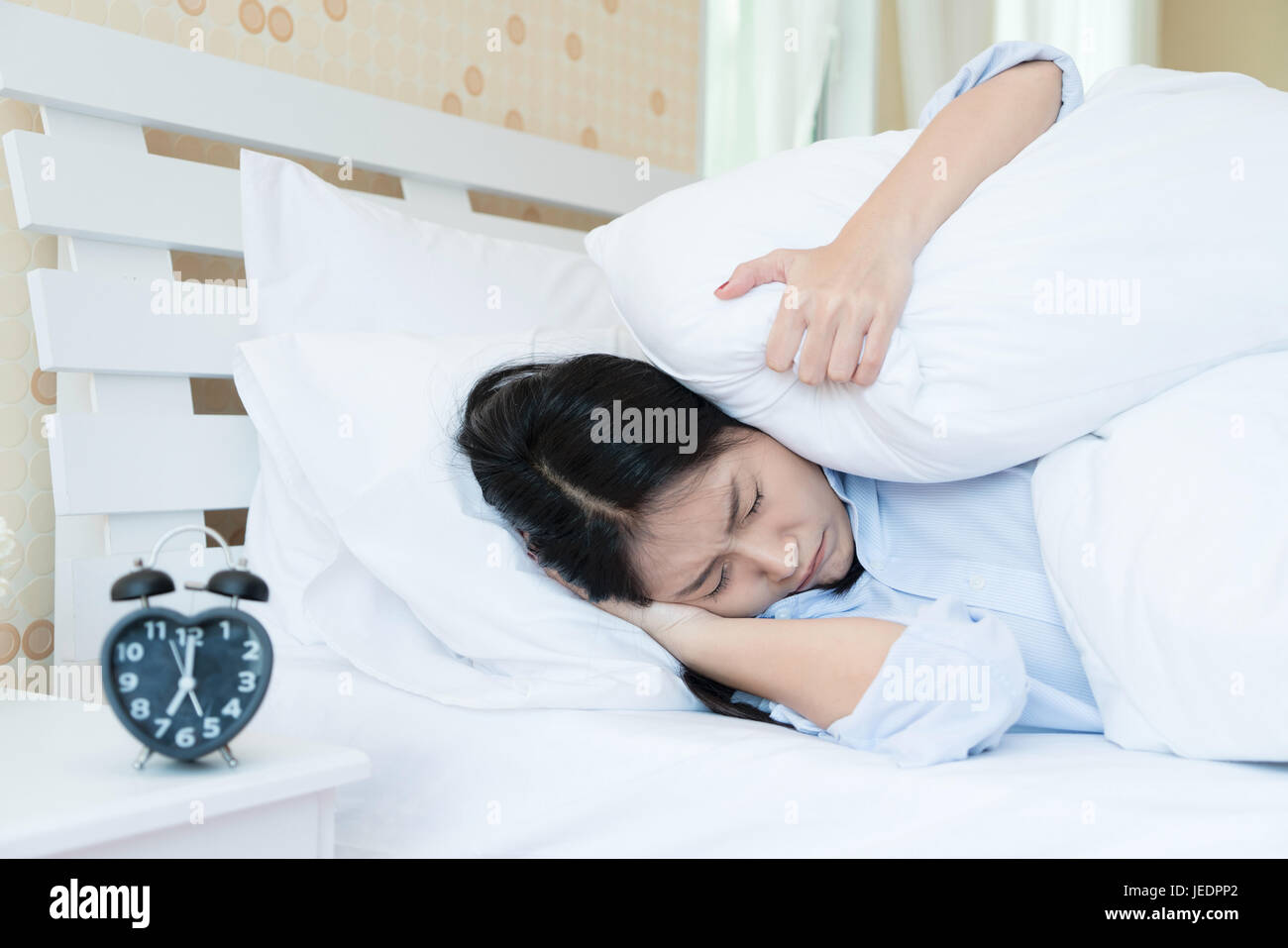 Young beautiful Asian woman lying in bed suffering from alarm clock ...