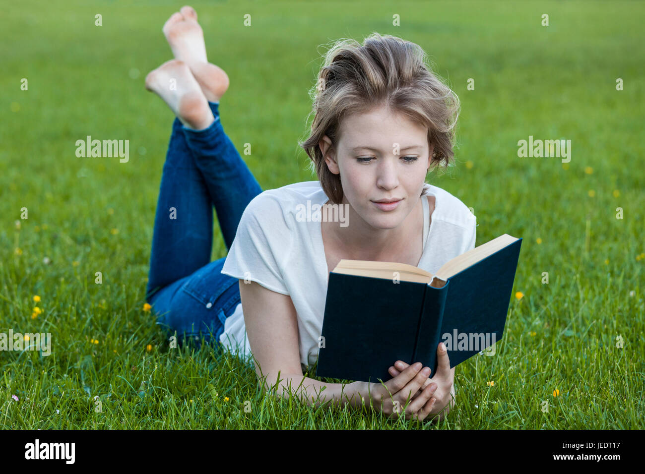 Barefoot young woman lying on a meadow reading a book Stock Photo - Alamy