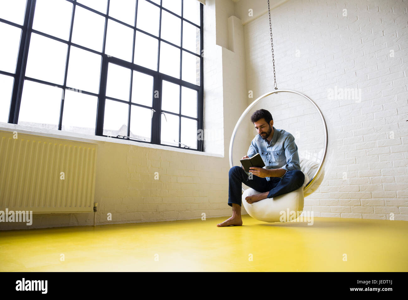 Young man sitting on swing in his loft reading a book Stock Photo - Alamy