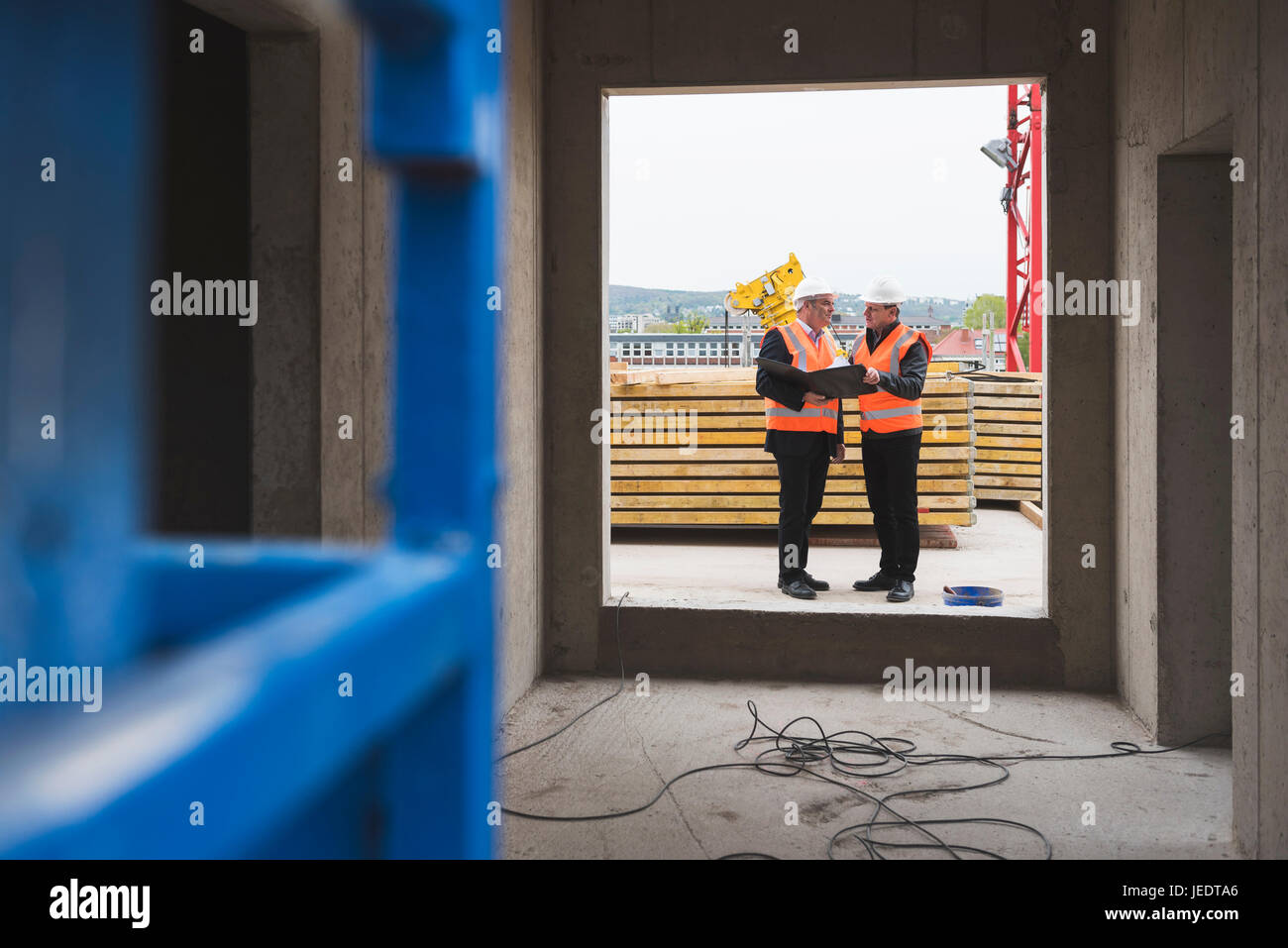 Two men wearing safety vests talking in building under construction ...