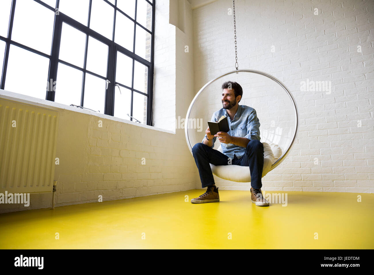 Young man with book sitting on swing in his loft Stock Photo - Alamy
