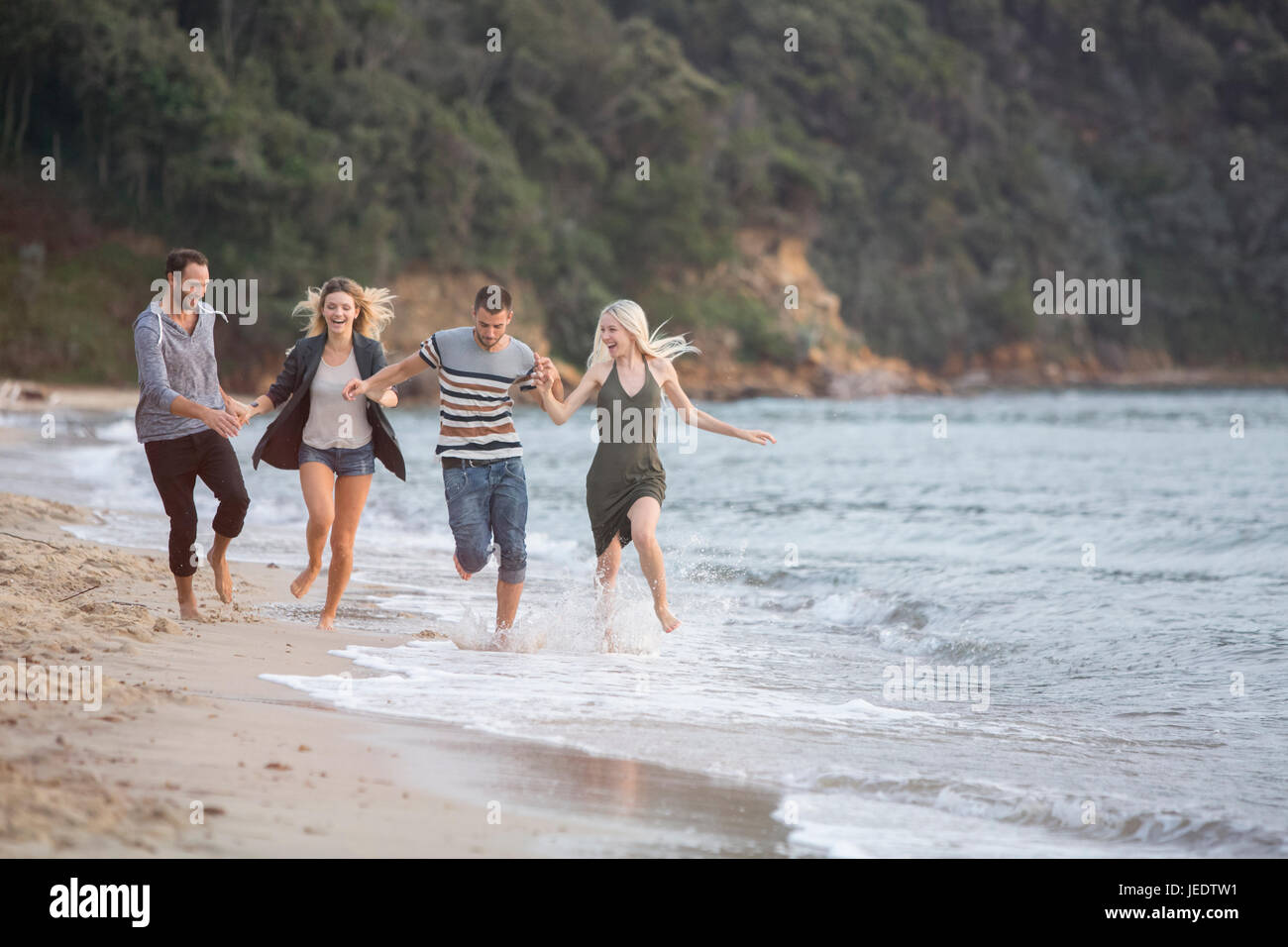 Four happy friends running at the beach Stock Photo - Alamy