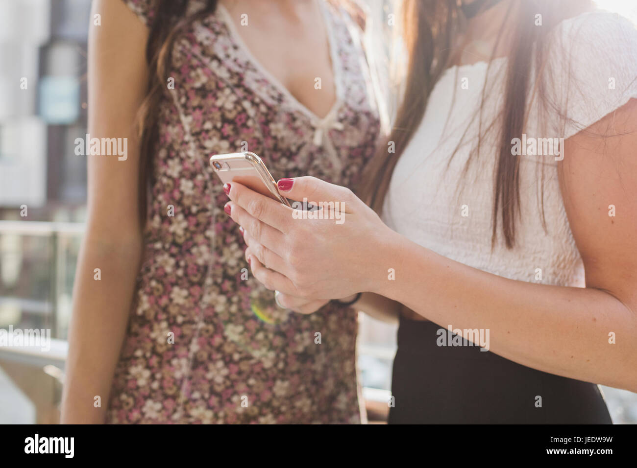 Two young women sharing cell phone in the city Stock Photo - Alamy