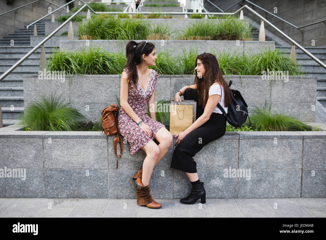 Two young women sitting down and talking in the city Stock Photo - Alamy