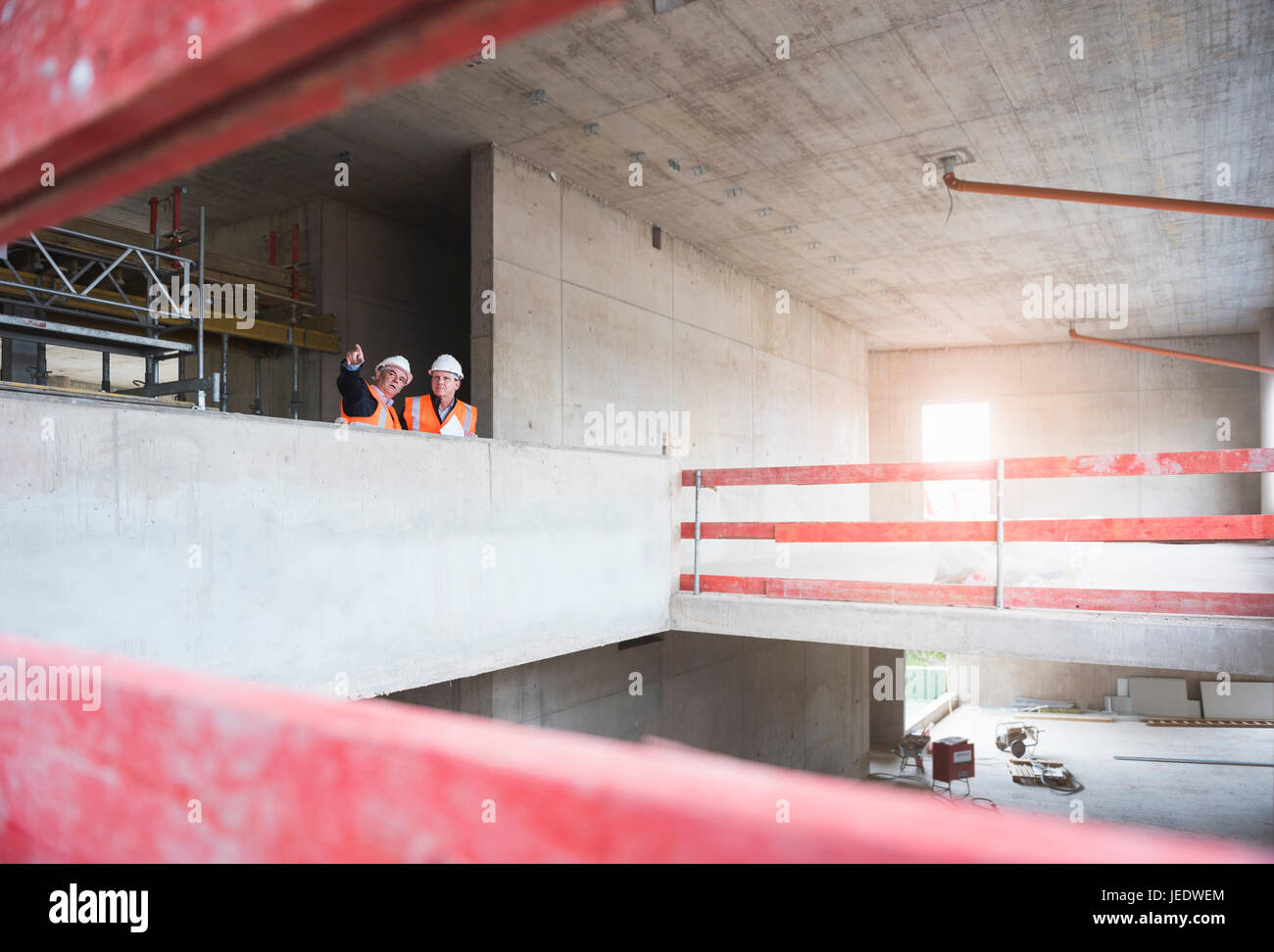 Two men wearing safety vests talking in building under construction ...
