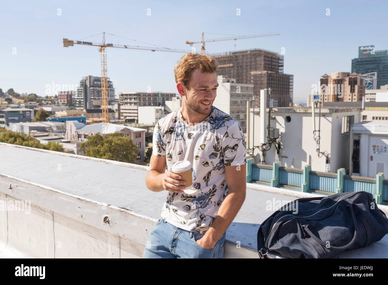 Young man standing on rooftop terrace drinking coffee Stock Photo - Alamy