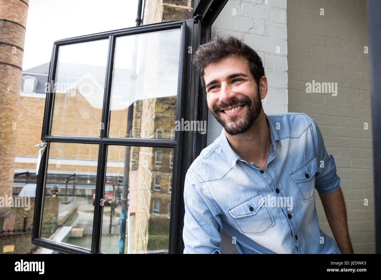 Portrait of smiling young man leaning out of the window Stock Photo - Alamy