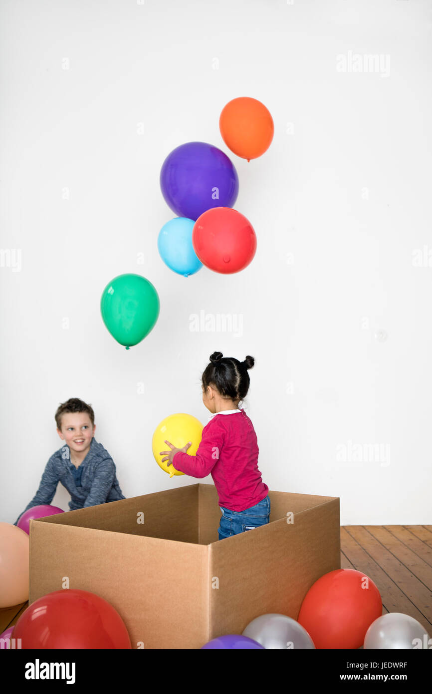 Two kids playing with balloon and cardboard box Stock Photo - Alamy