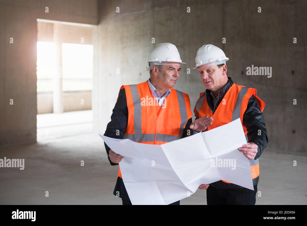 Two men with plan wearing safety vests talking in building under ...
