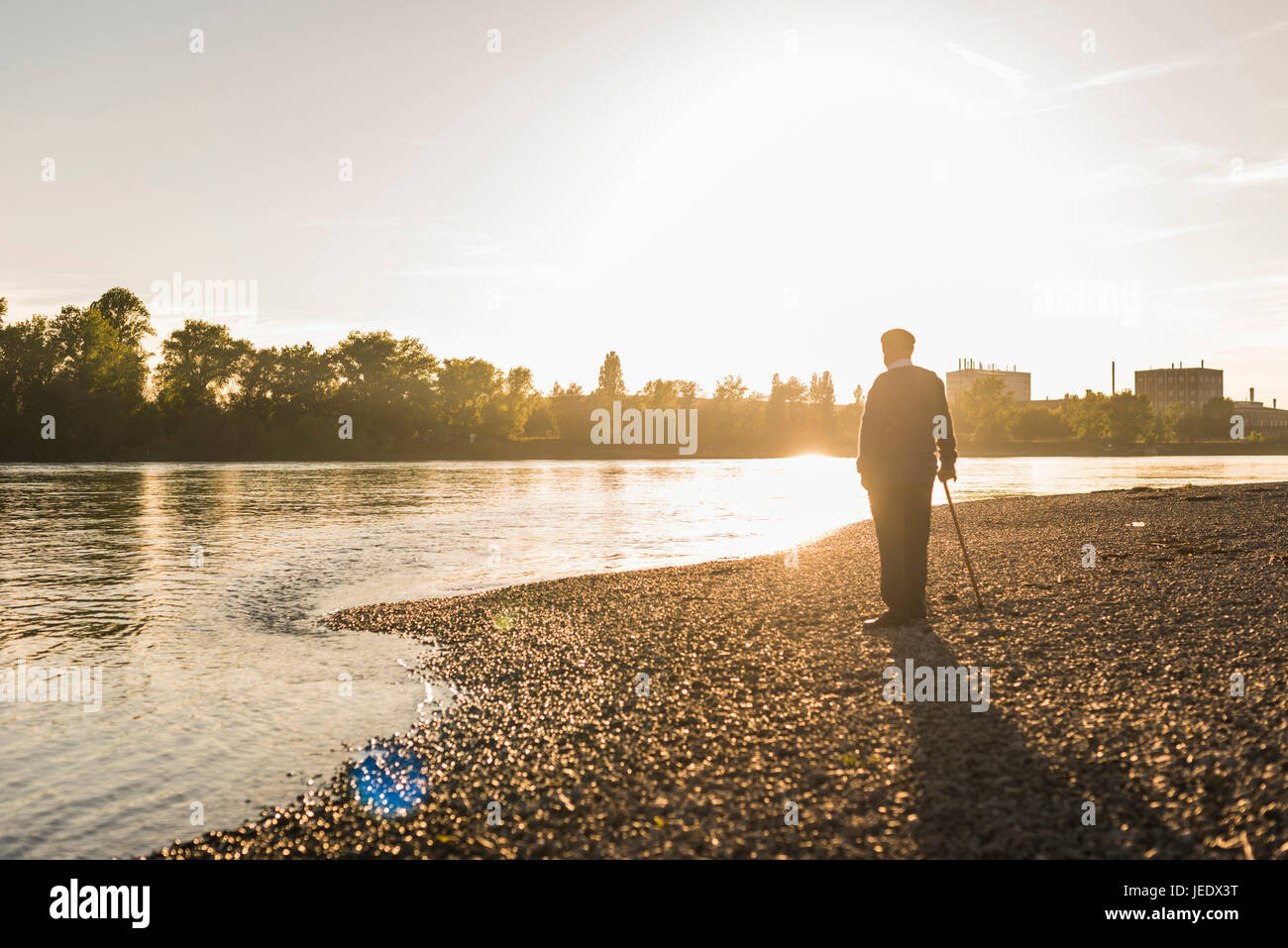 Back view of senior man standing at riverside watching sunset Stock ...