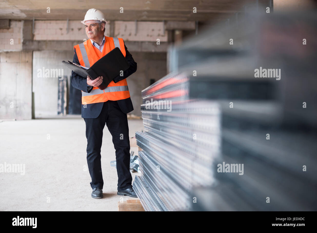 Man with documents wearing safety vest in building under construction ...