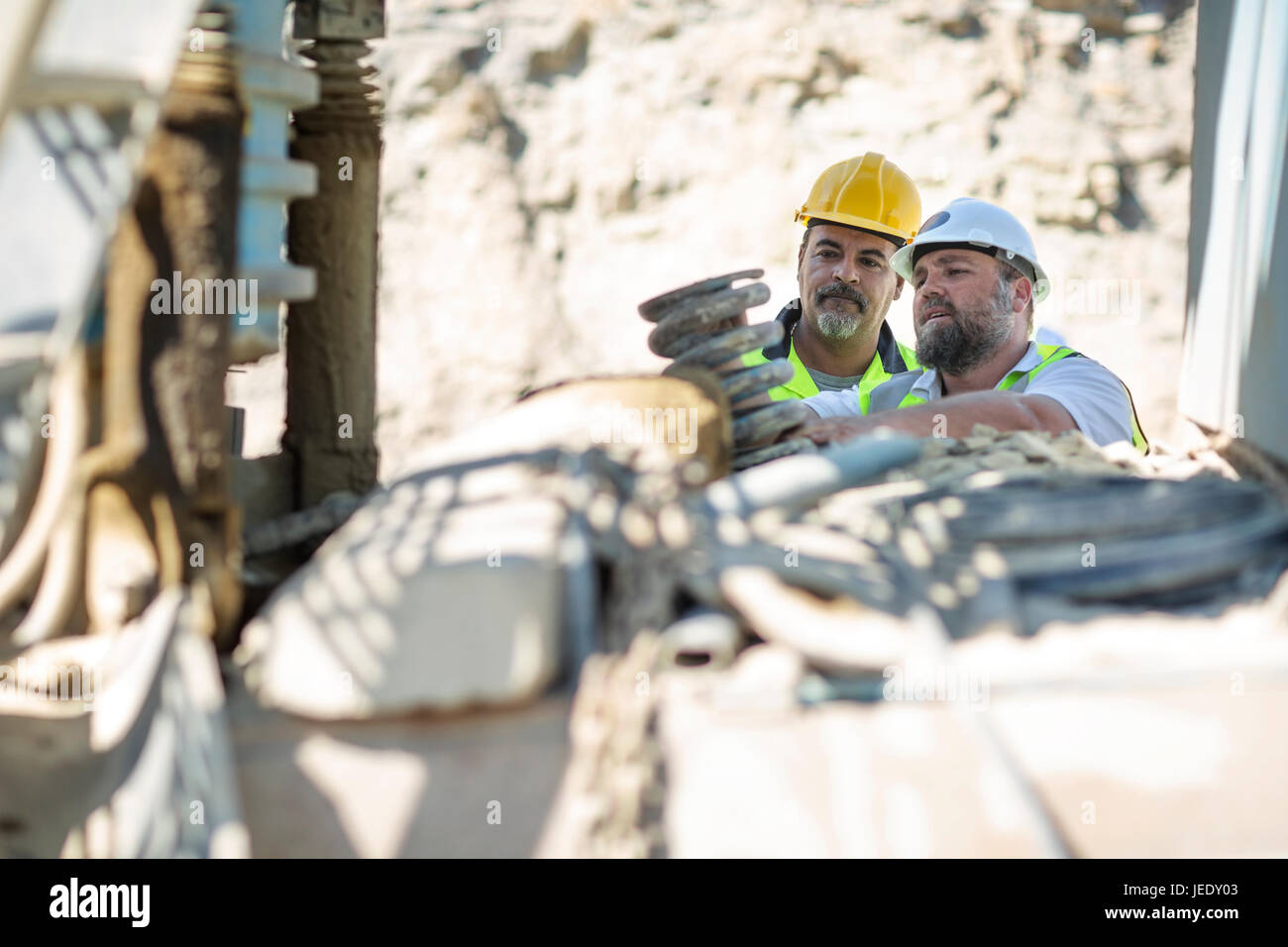 Two quarry worker standing at digger, talking Stock Photo - Alamy
