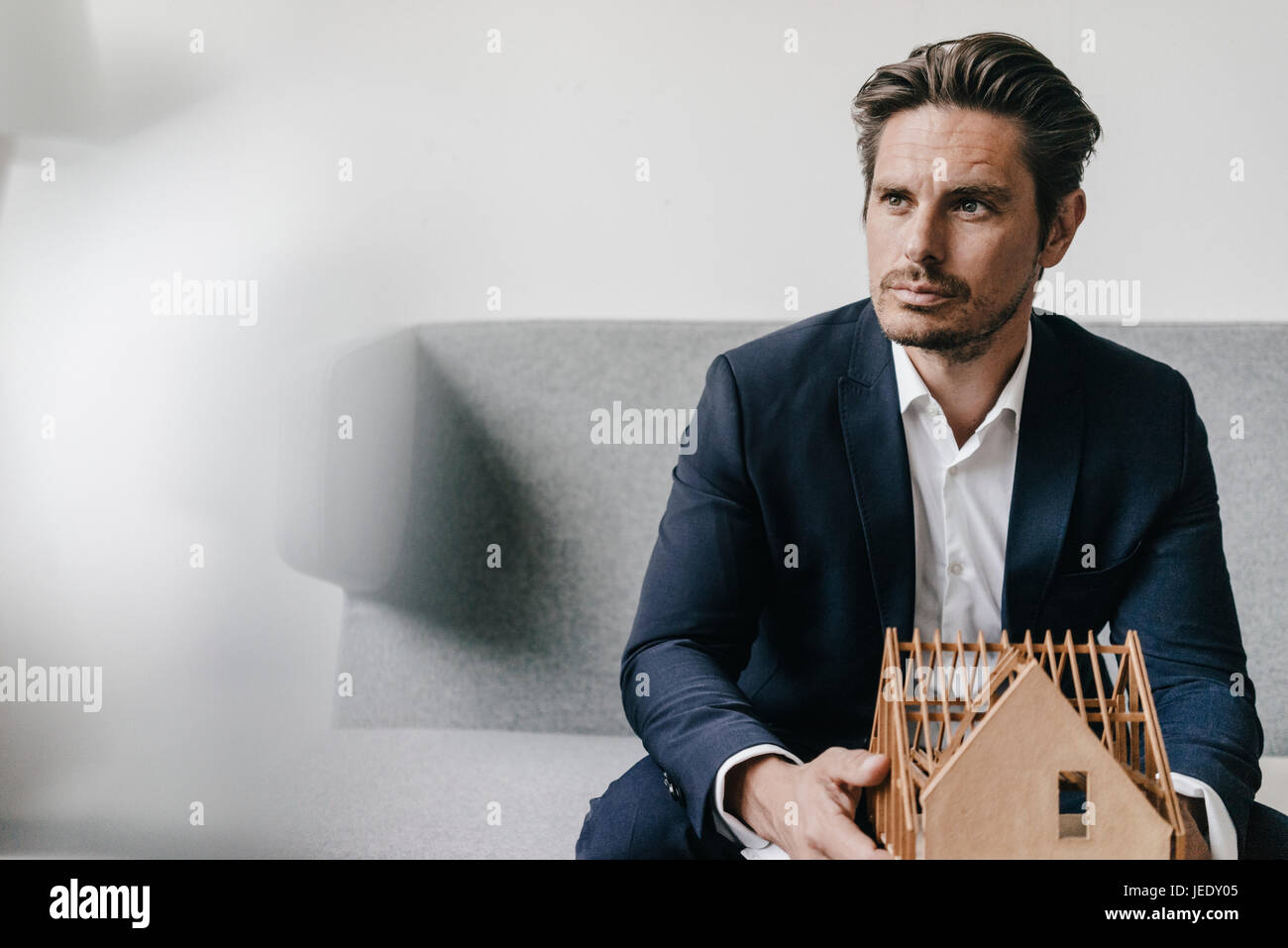 Architect holding architectural model thinking Stock Photo - Alamy