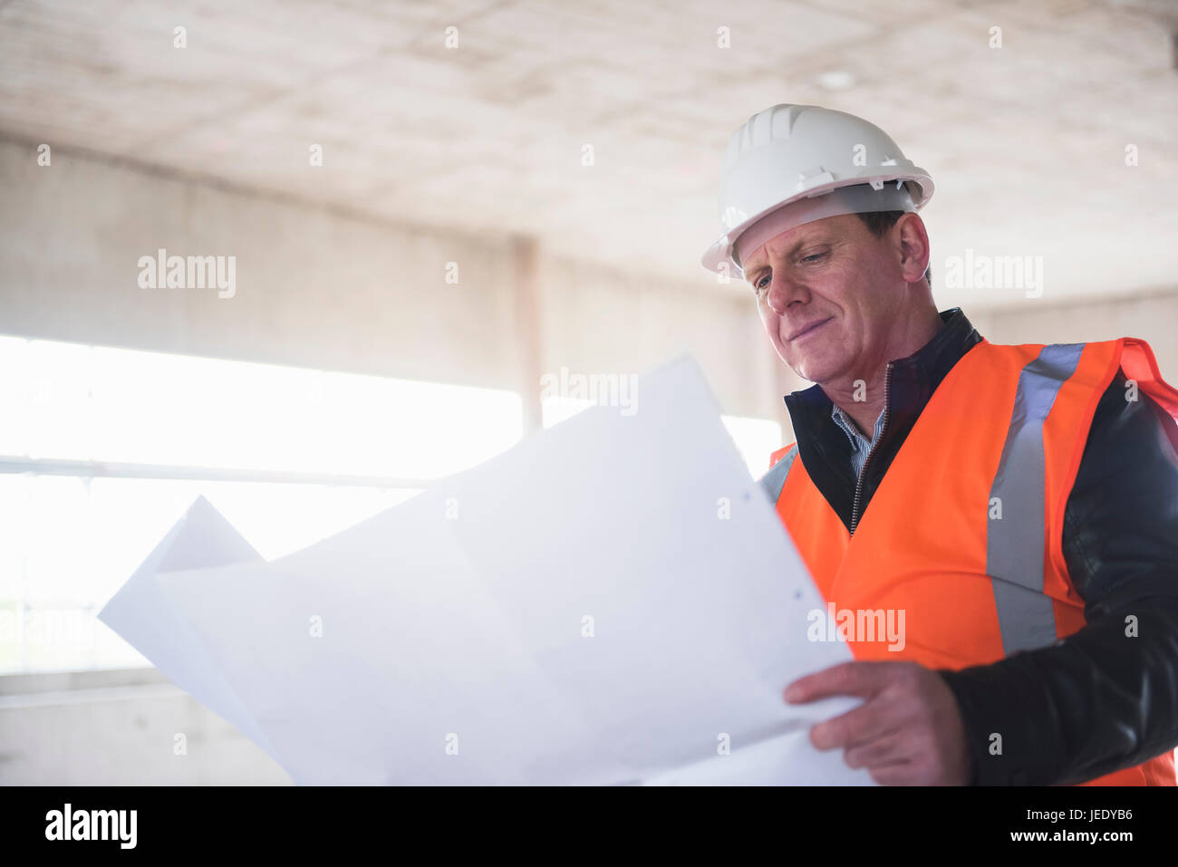 Man with plan wearing safety vest in building under construction Stock ...