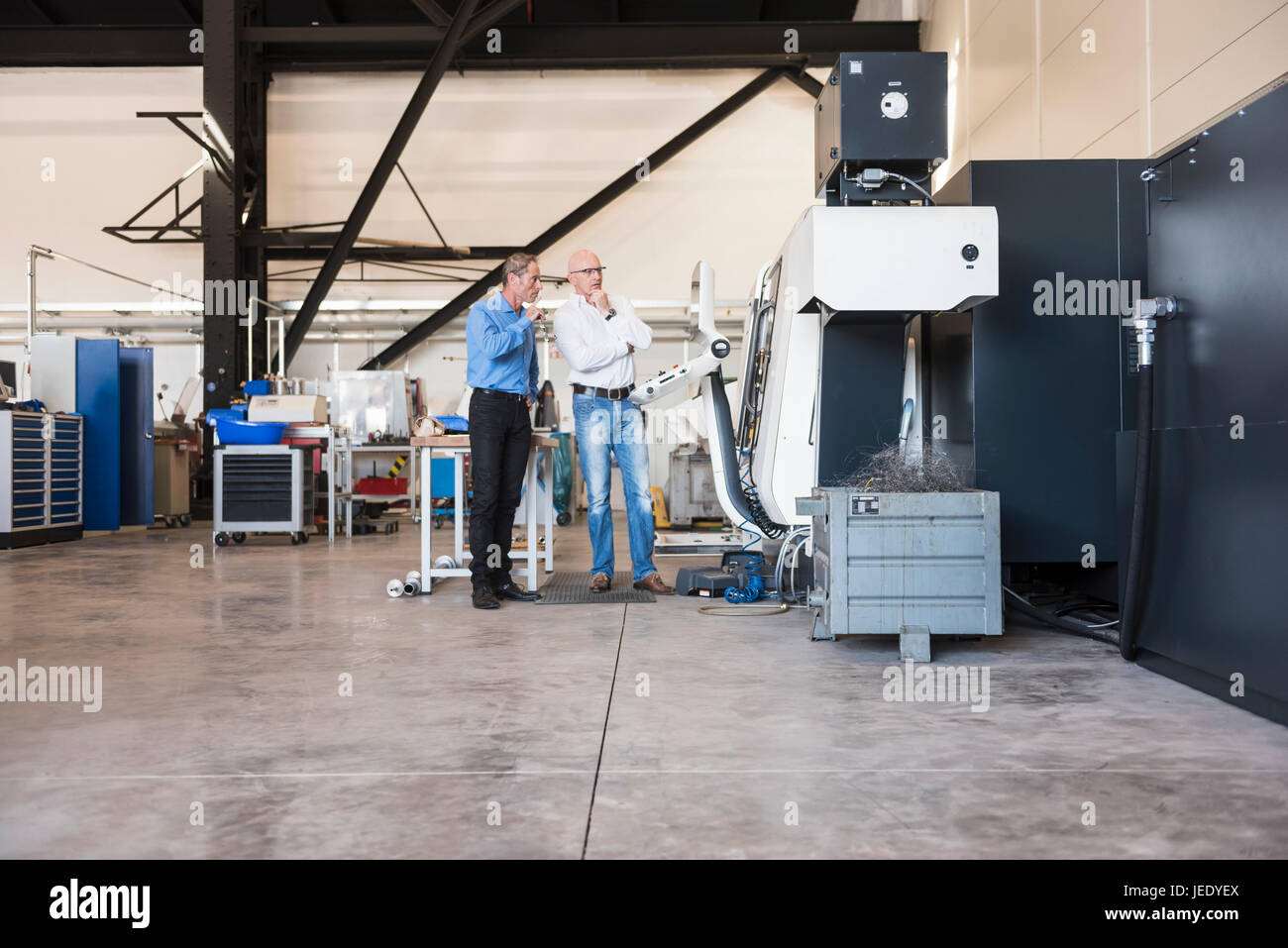 Two men talking at machine on factory shop floor Stock Photo - Alamy