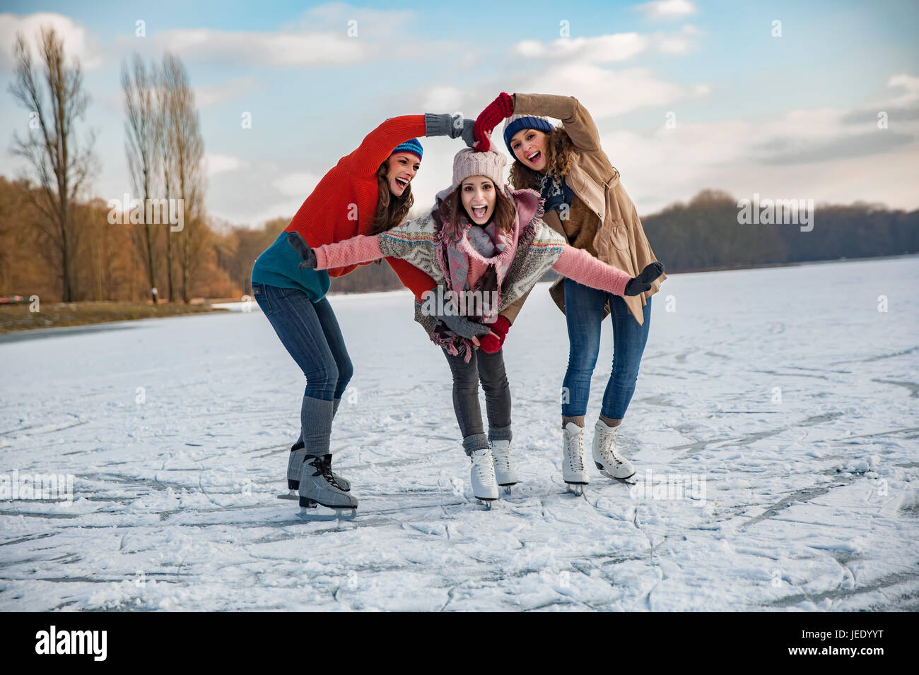 Three female friends ice skating and shaping a heart with their arms ...