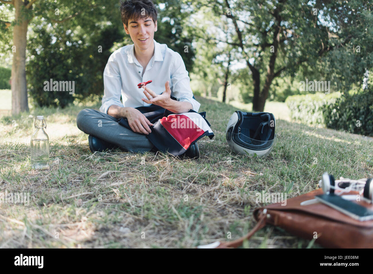 Young man sitting on meadow in park using a fidget spinner Stock Photo ...