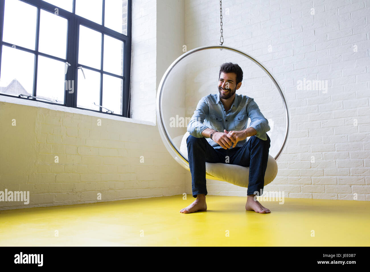 Smiling young man sitting on swing in his loft Stock Photo - Alamy