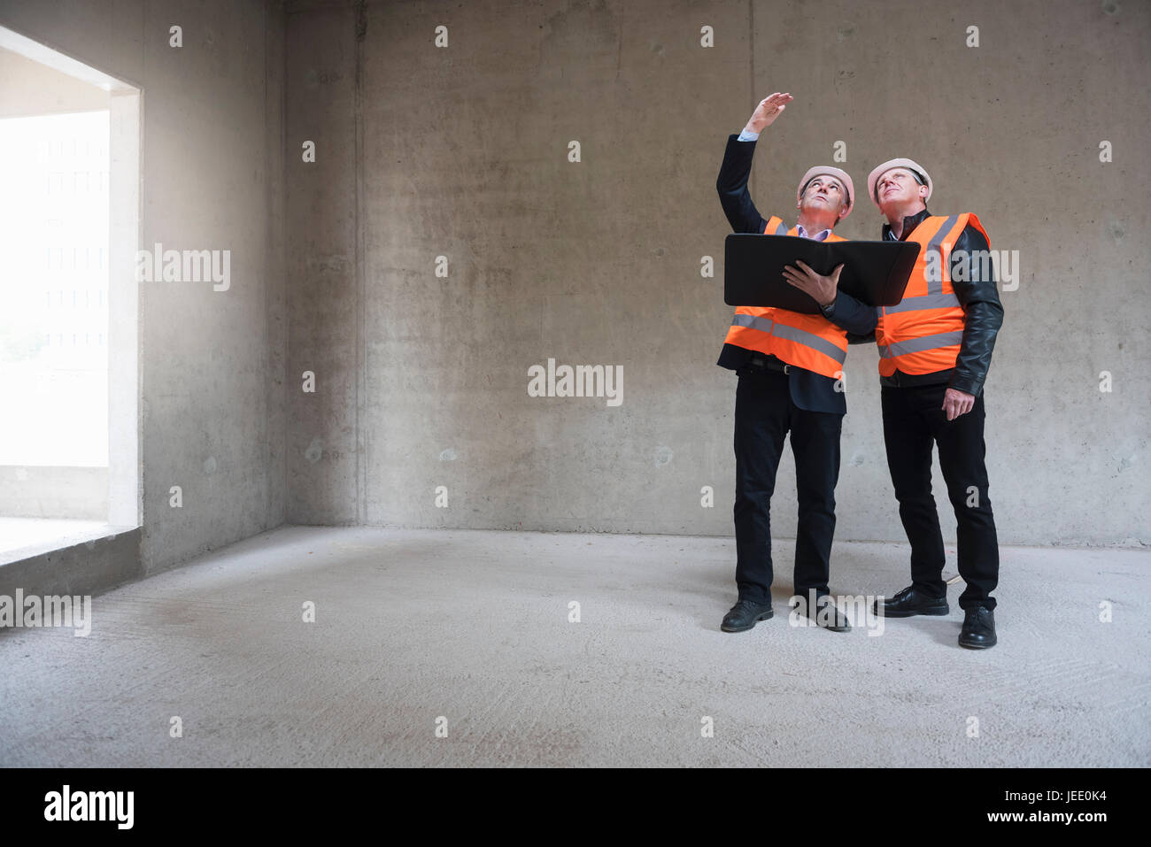 Two men wearing safety vests talking in building under construction ...