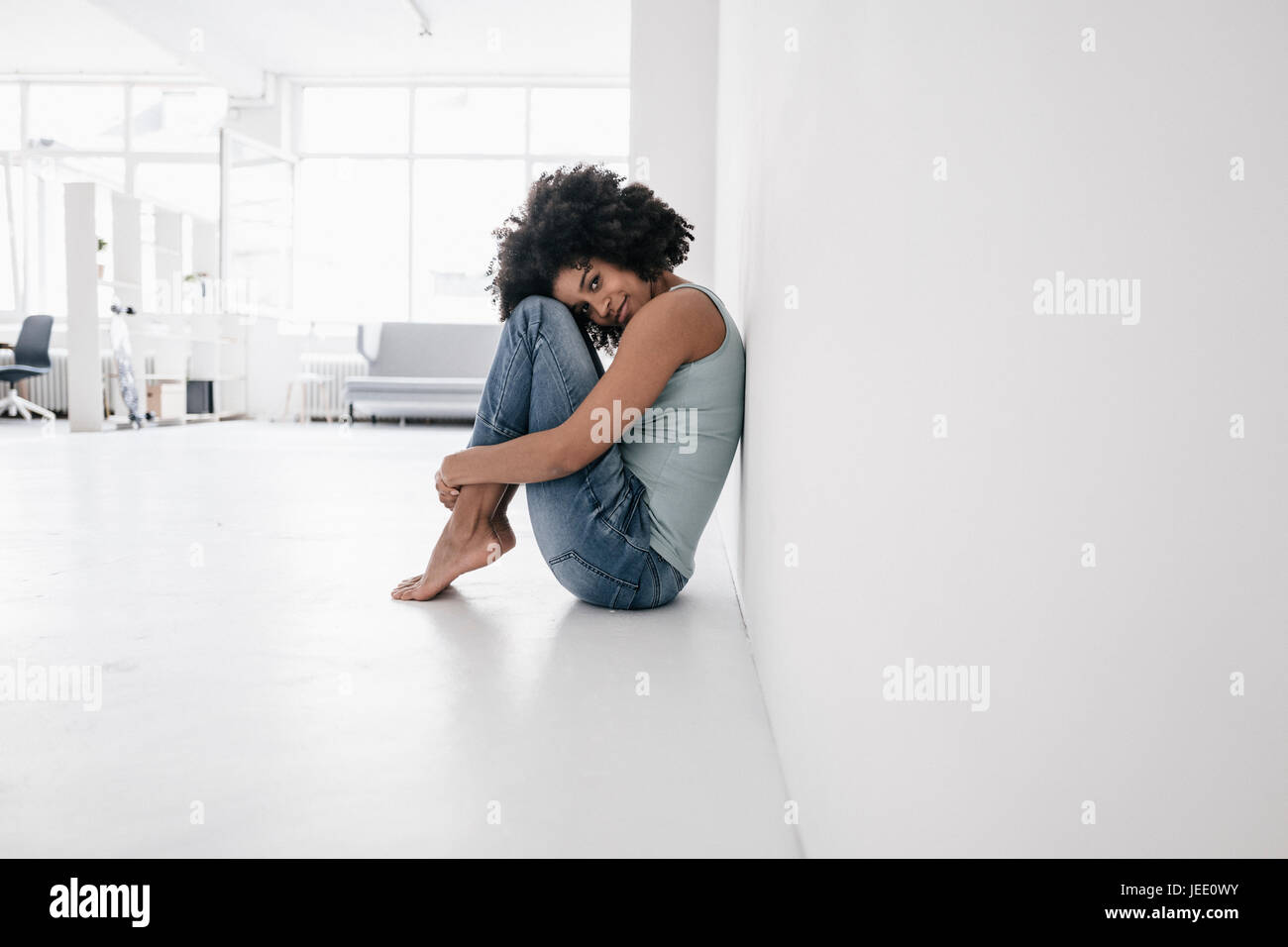 Young woman sitting on floor, hugging knees Stock Photo - Alamy
