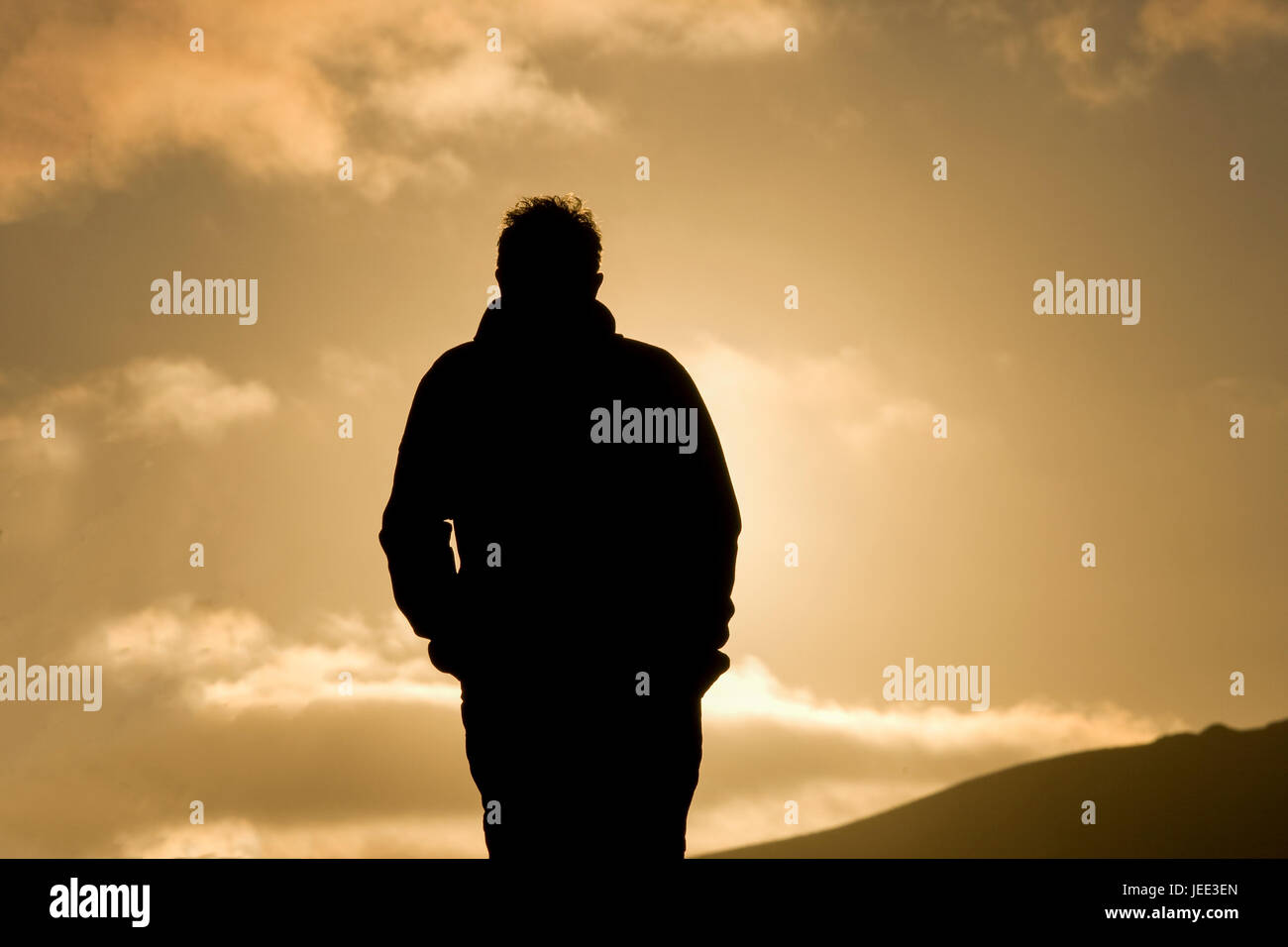 Man walking in sunset with hands in pocket. Black silhouette against ...