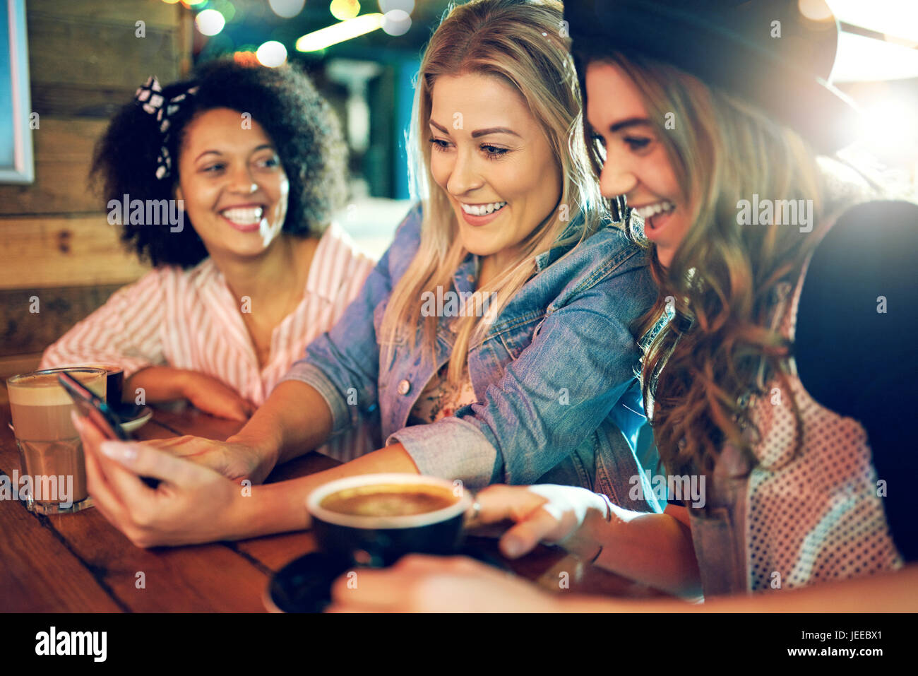 Three young women laughing and joking together as they look at ...