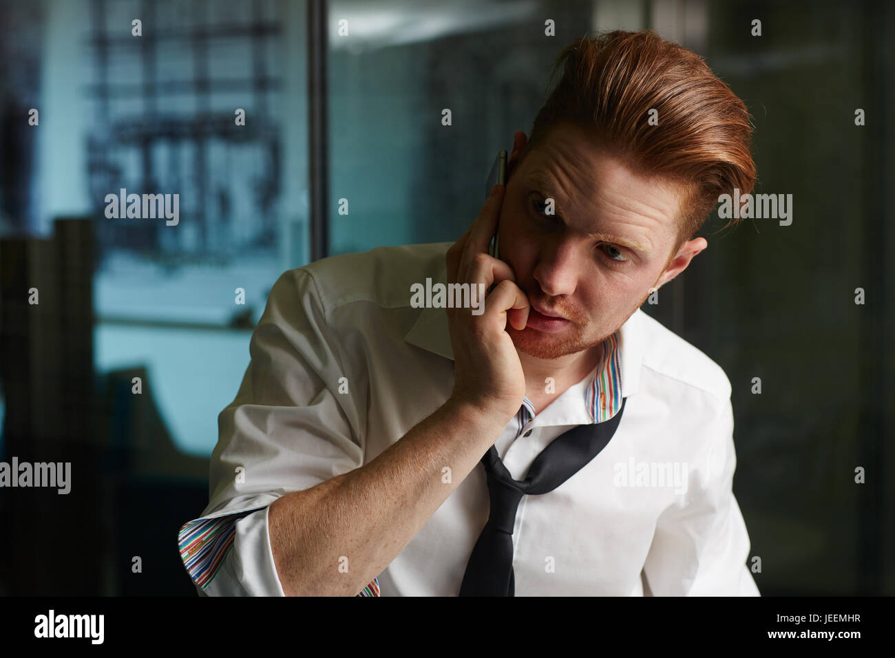 Overworked man talking on cellphone late in the evening in office Stock ...