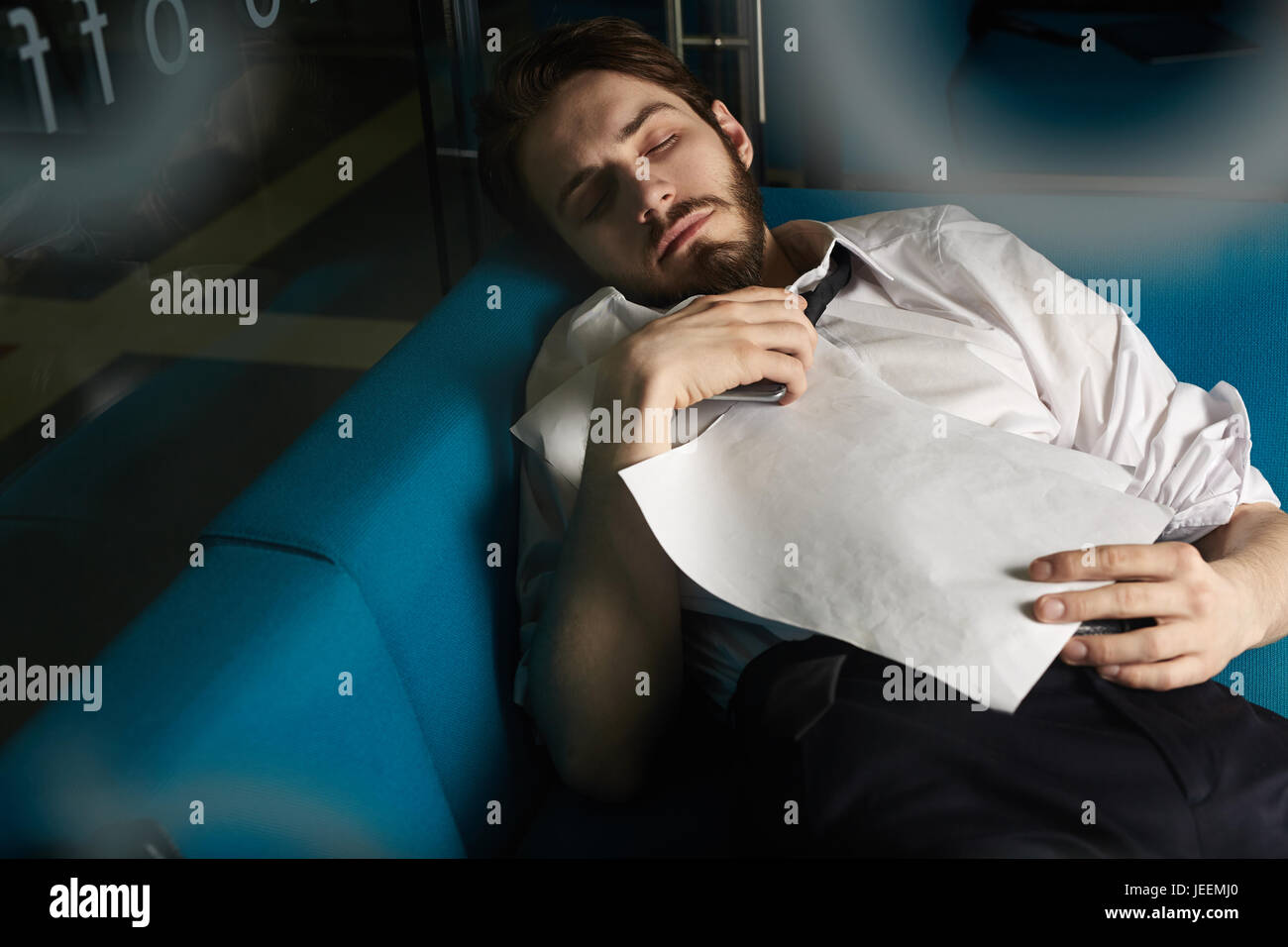 Overworked banker with smartphone and paper asleep on sofa in his ...