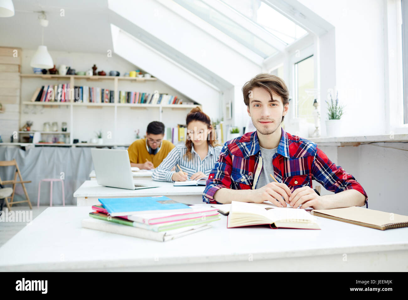 Young learner sitting by desk with groupmates behind Stock Photo - Alamy