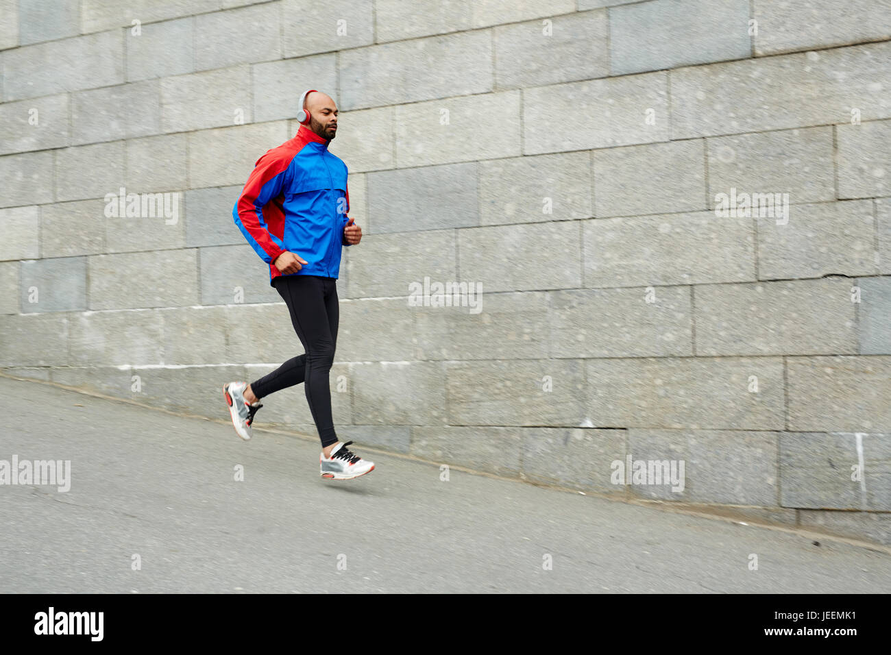 Young sprinter with headphones running along wall Stock Photo - Alamy