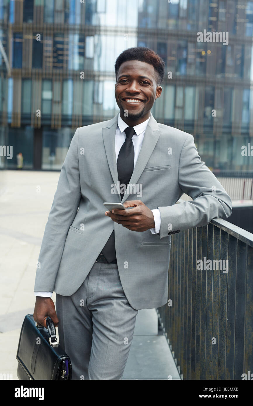 Happy young agent with briefcase and smartphone looking at camera in ...