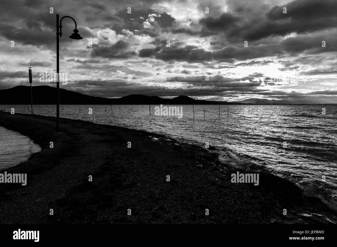 A lake shore near sunset, with lamp post, water reflections and ...