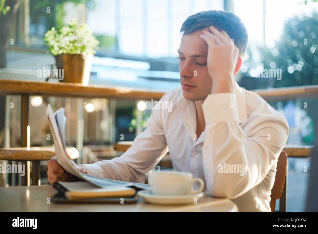 Thoughtful man reading a newspaper in a street cafe at lunch. Concept ...