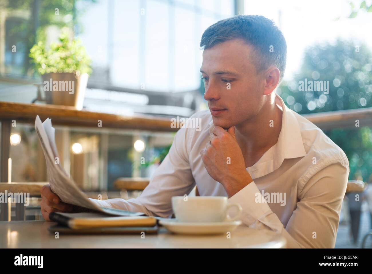 Thoughtful man reading a newspaper in a street cafe at lunch. Concept ...
