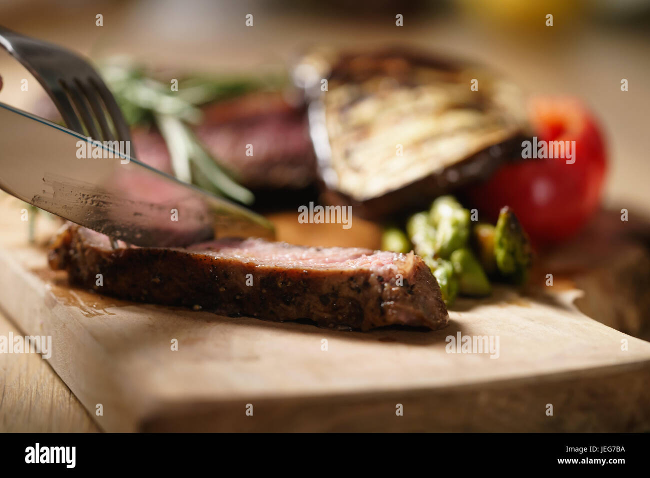 slicing medium rib eye steak with grilled vegetables, shallow focus ...