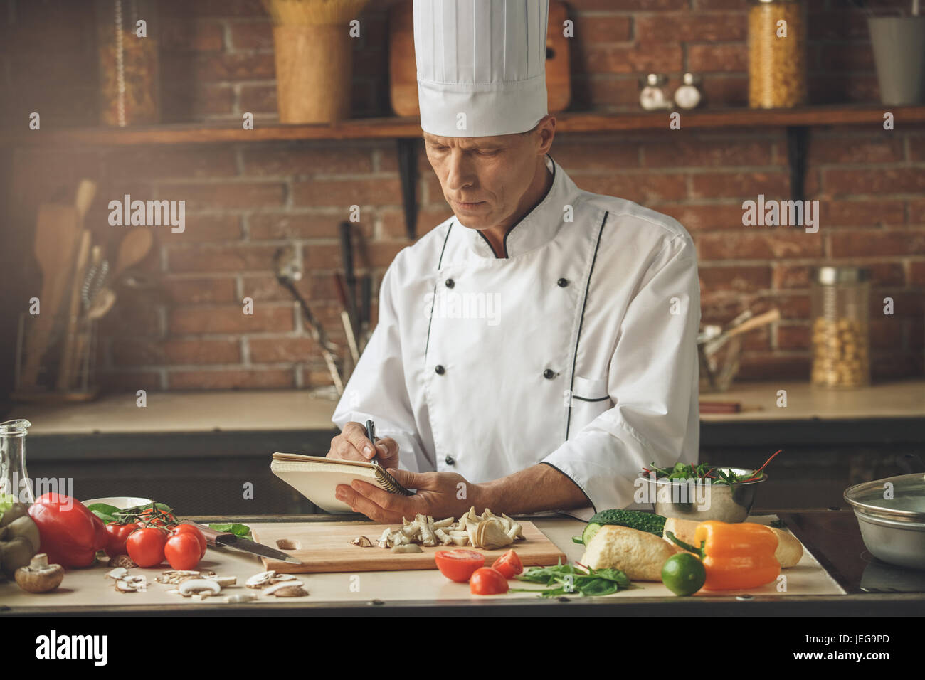 Mature male professional chef cooking meal indoors writing receipt ...