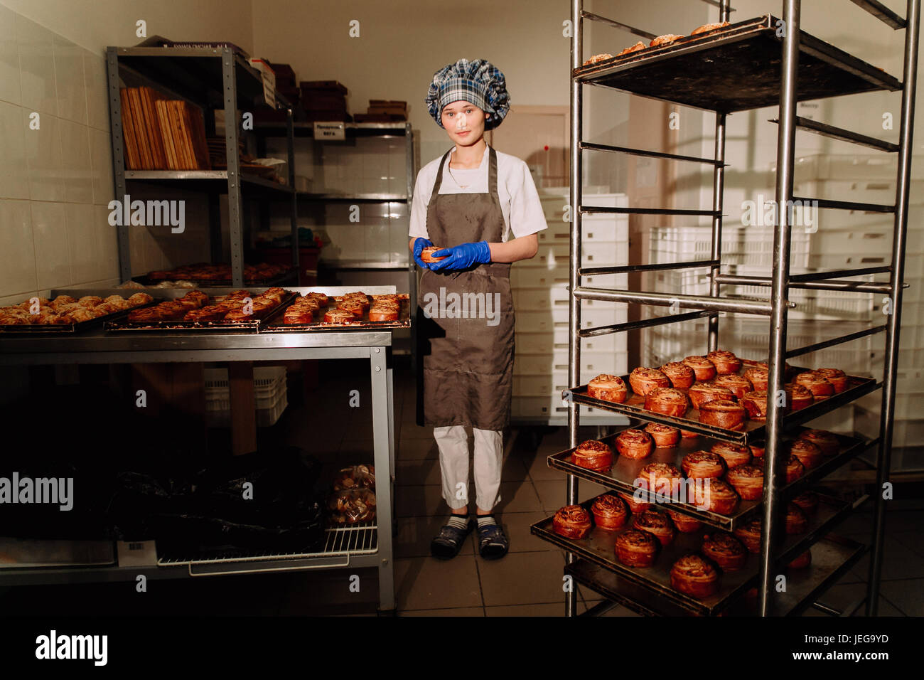 baker standing in his bakery in the morning and is baking bread or buns ...