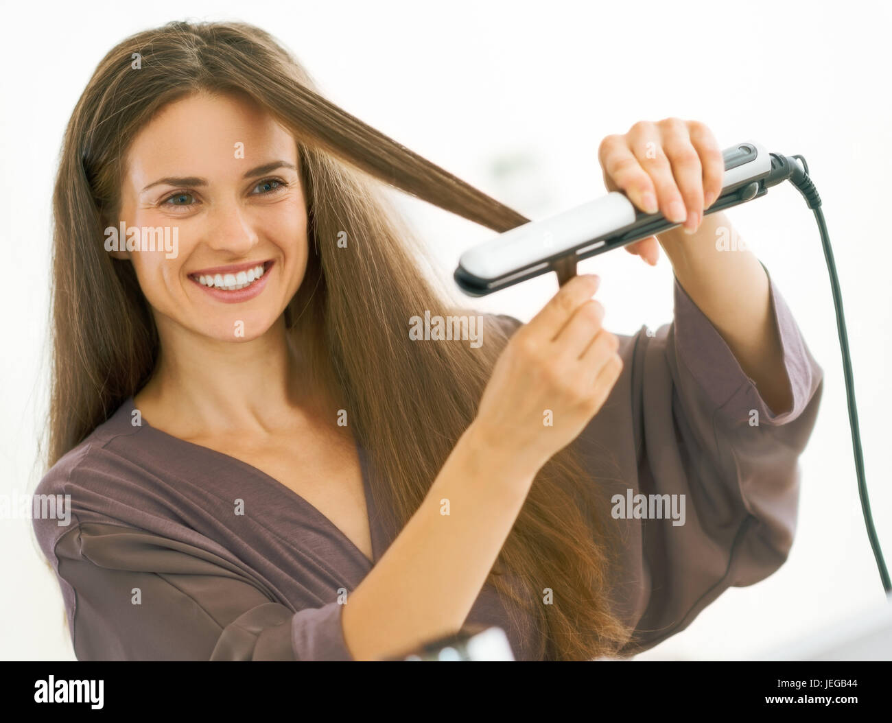 Happy young woman straightening hair with straightener Stock Photo - Alamy