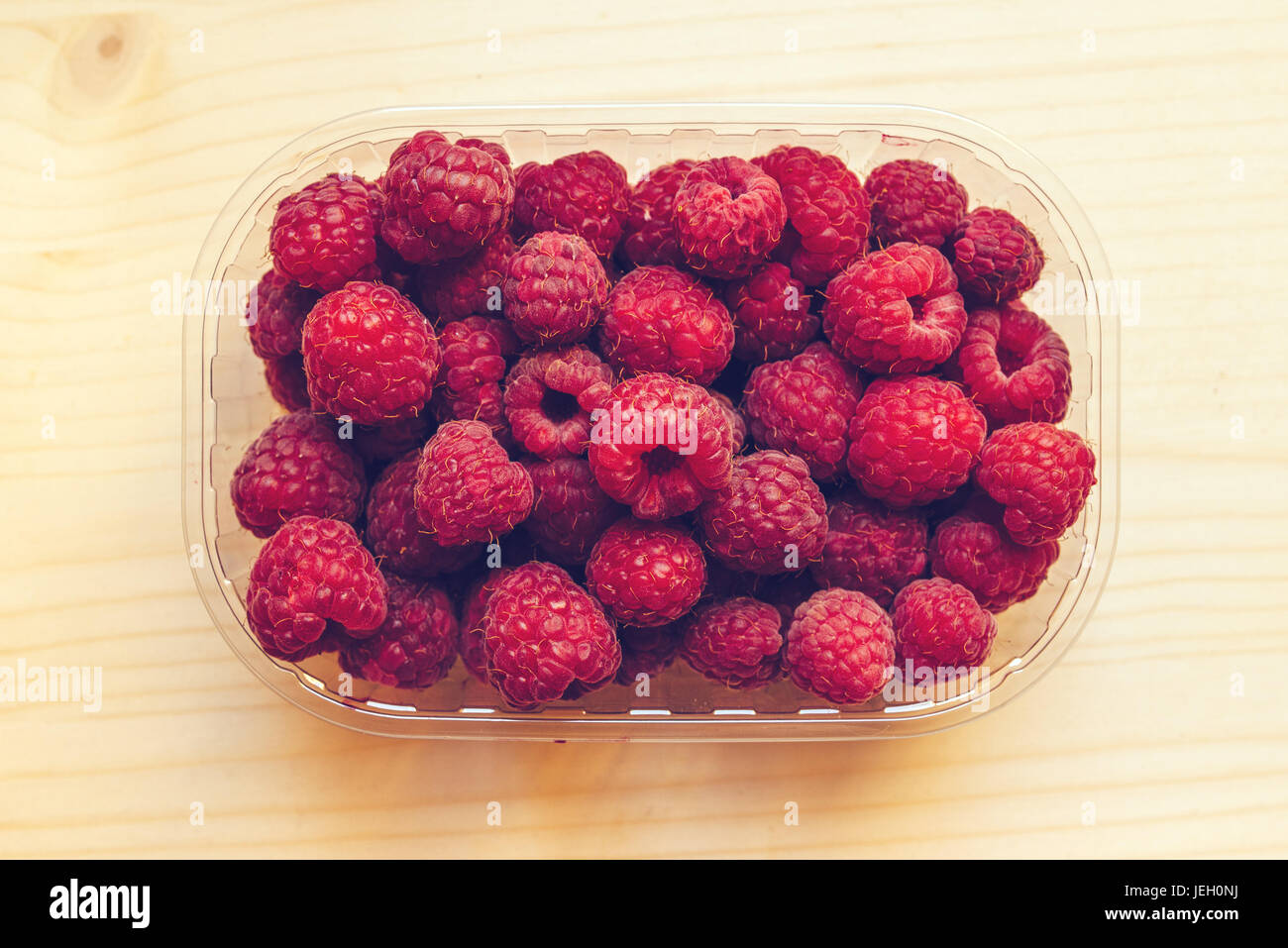 Top view of ripe raspberries in plastic container box on wooden table ...