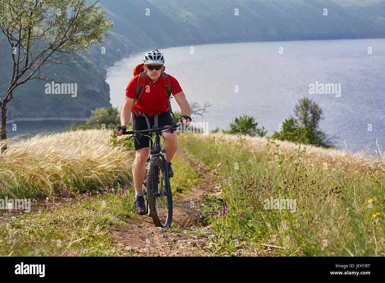 Young cyclist cycling in the green summer meadow against beautiful ...