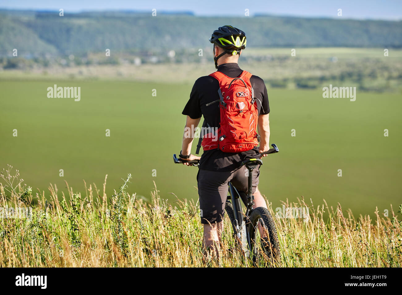 Rear view of the cyclist standing with mountain bike against beautiful ...