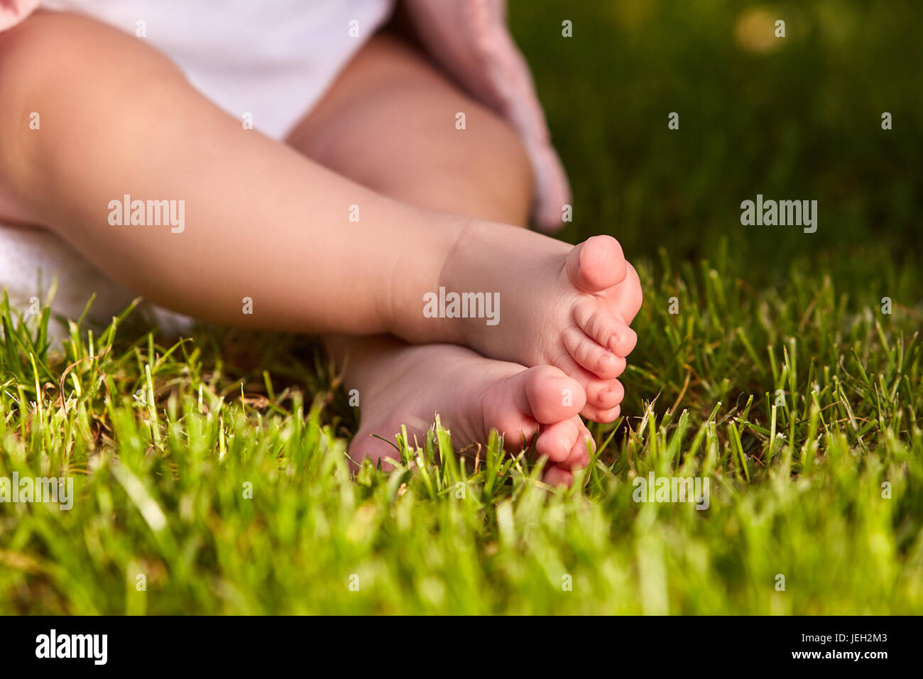 Small baby feet on the green grass at summer sunshiny day in the park ...