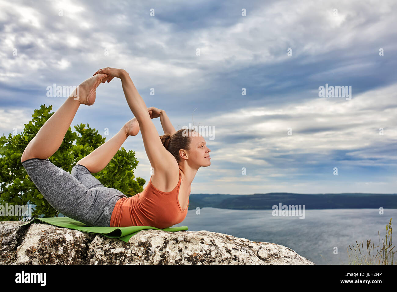 Young sportive woman training yoga on rock against beautiful big river ...